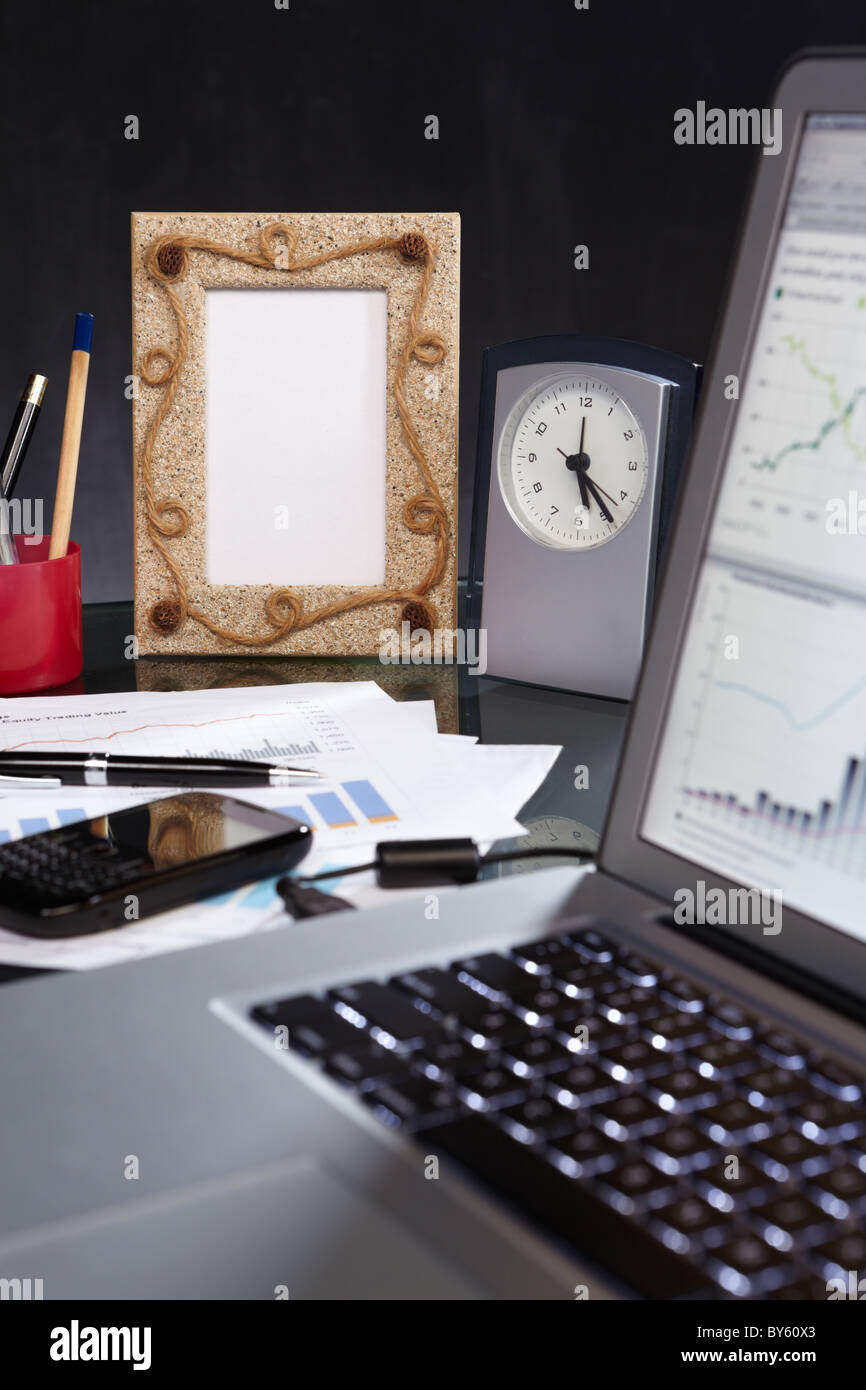 Office desk full of stuff: laptop, clock, document, blank frame and ...