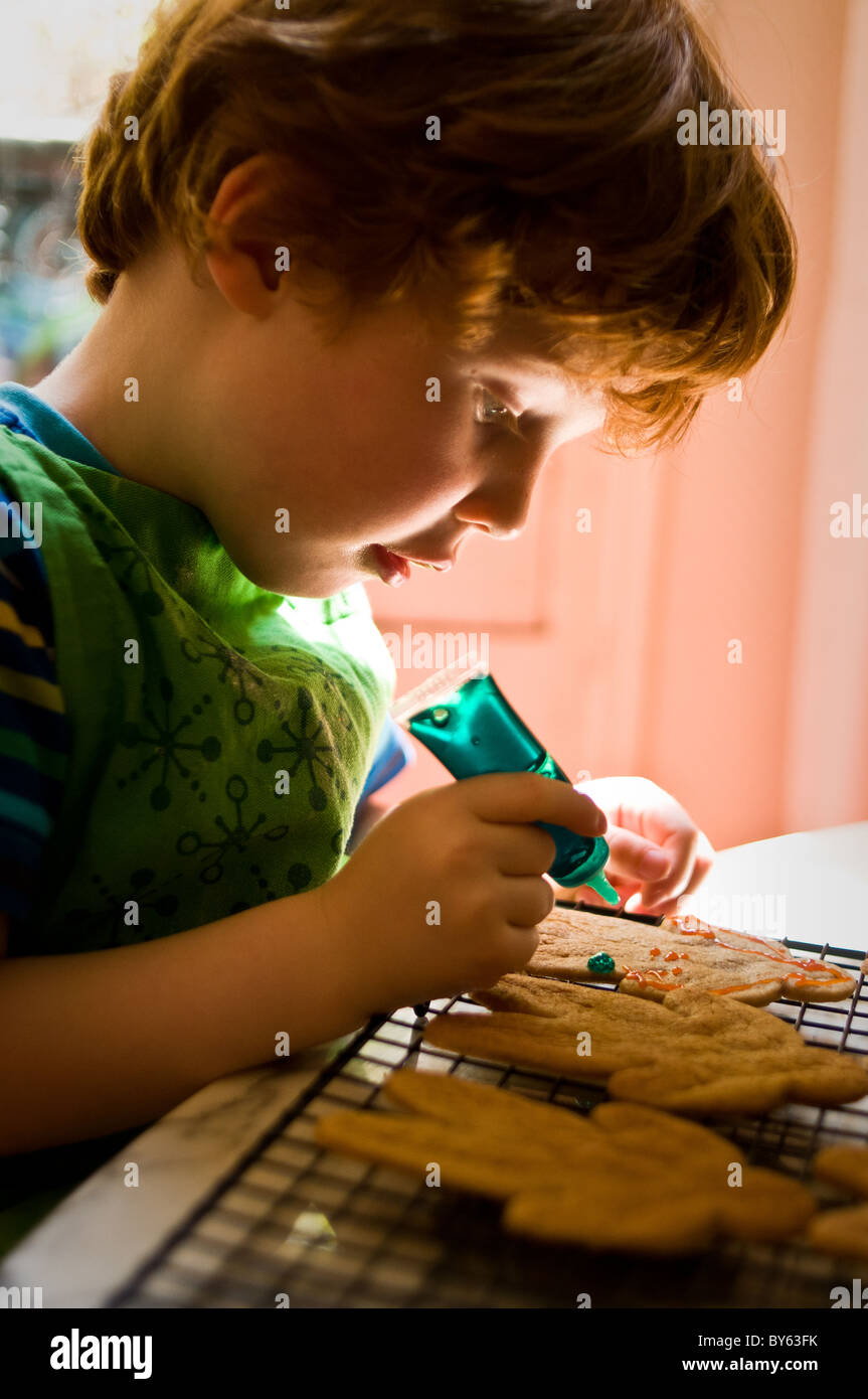 A young boy decorating gingerbread men that he has just made Stock ...