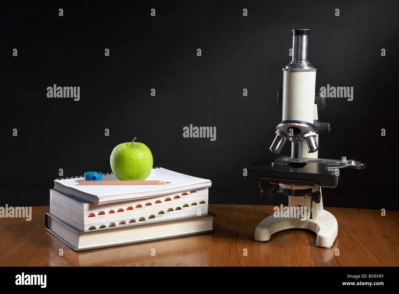 Biology class concept with green apple on pile of books and microscope ...