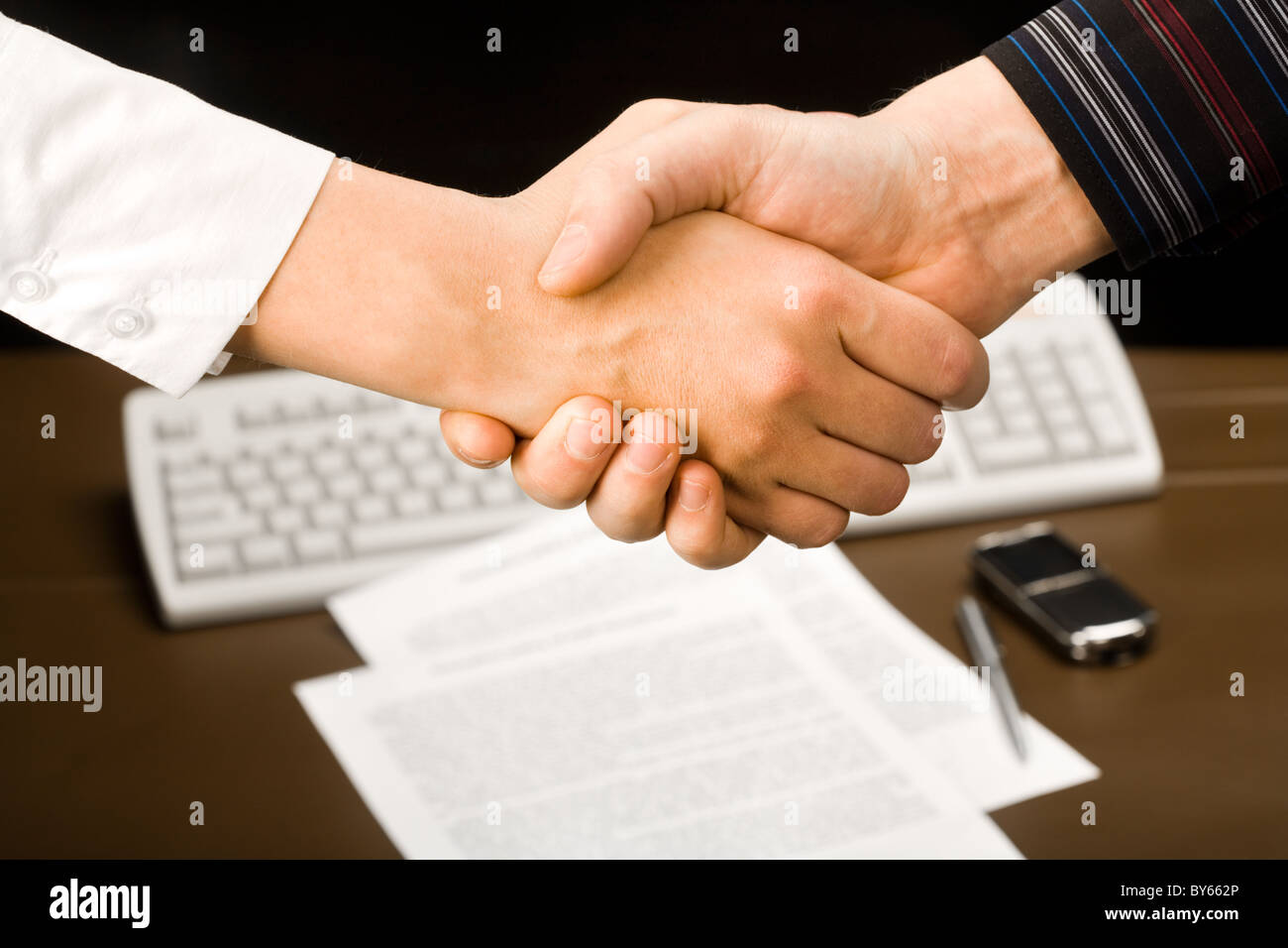 View of handshake over paper, keyboard, pen, phone in the background ...