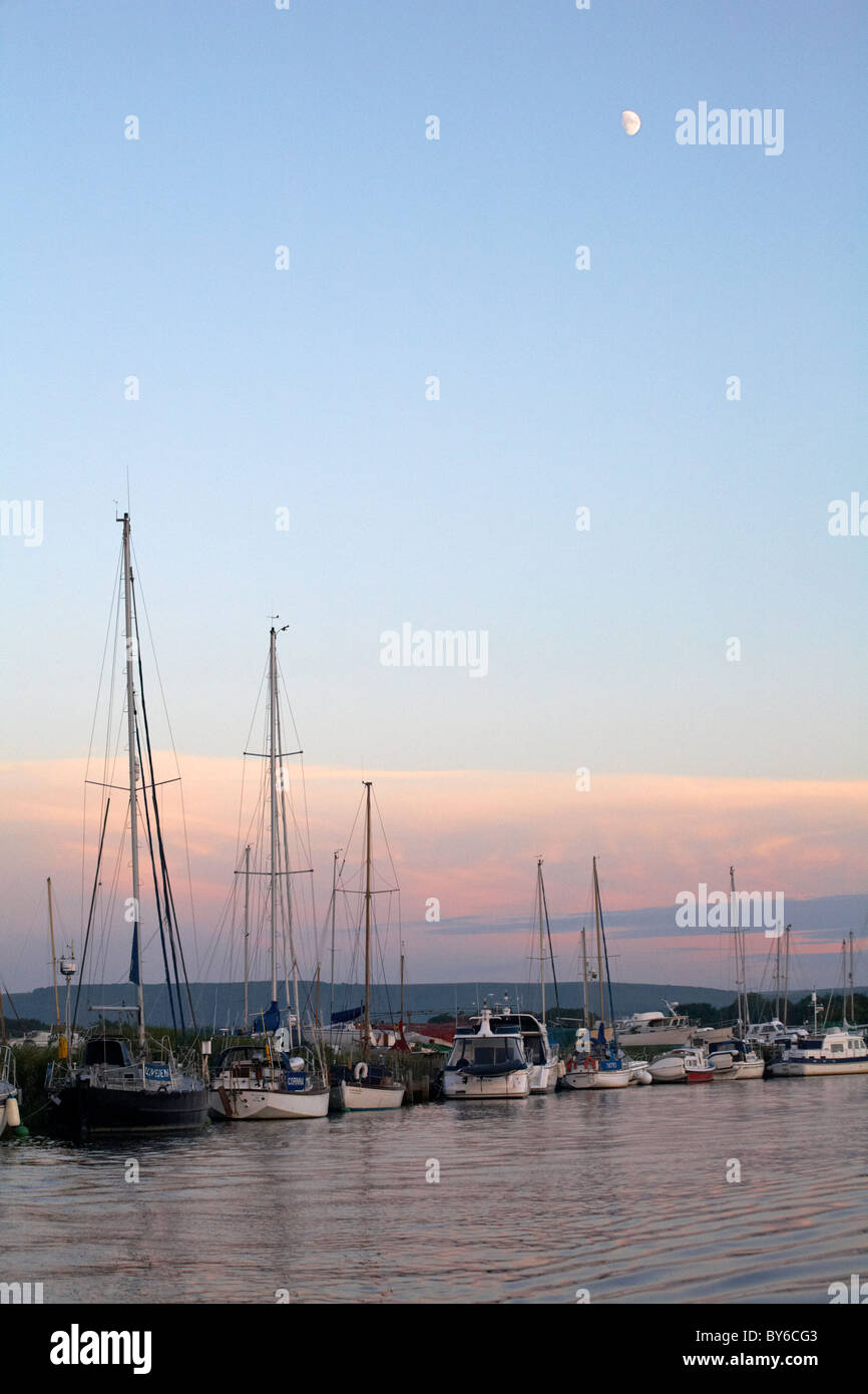 Boats moored along Wareham river on a Summer evening with the moon out ...