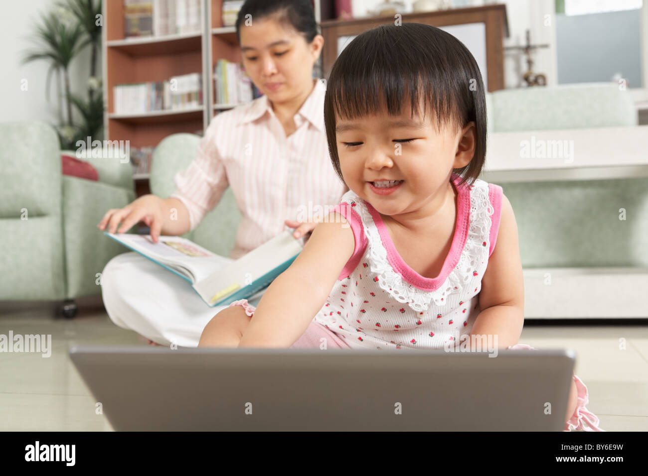 LIttle girl playing laptop with her mother or nanny on background ...