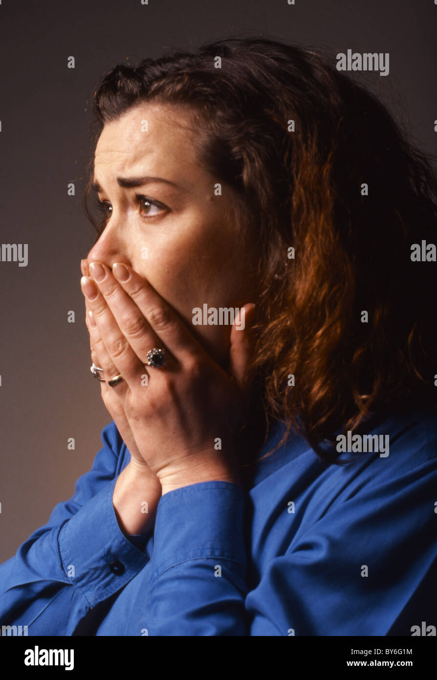 Woman with a very worried look fearful, hands clasped to her face ...