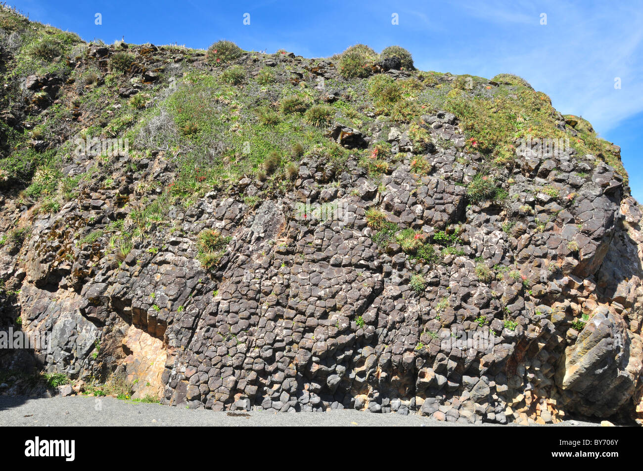 Blue sky sunny black basalt cliff, with sub-vertical polygonal columns ...