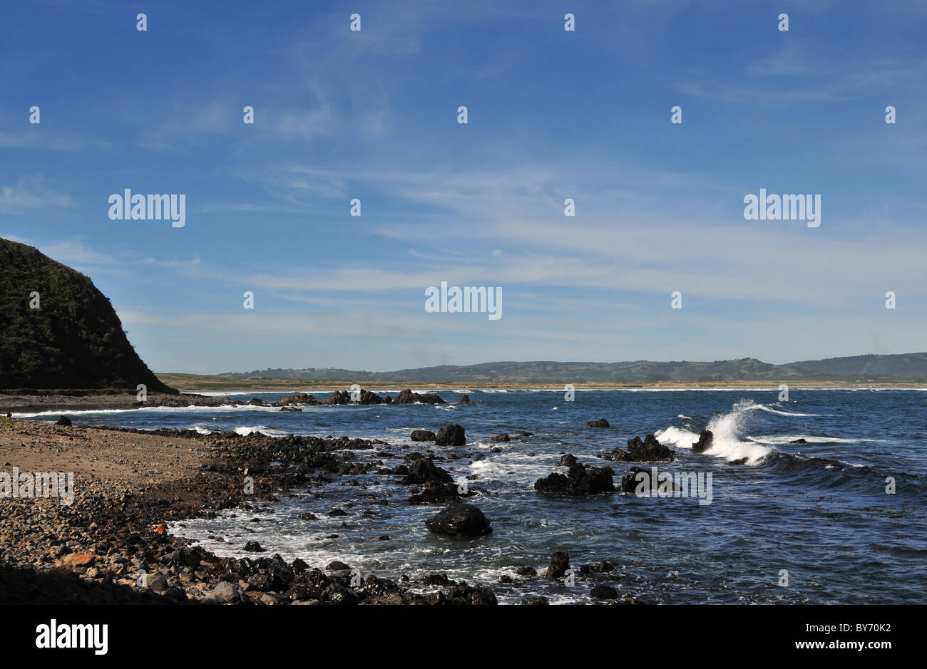 Blue sky inland view of a white breaker on basalt beach below cliffs ...
