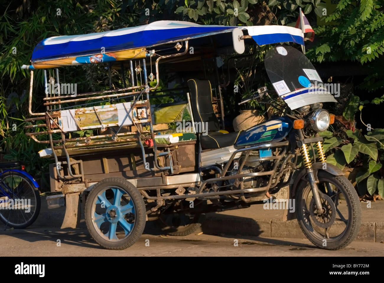 A colorful tuk-tuk with blue wheels is parked on a city street in Nong ...