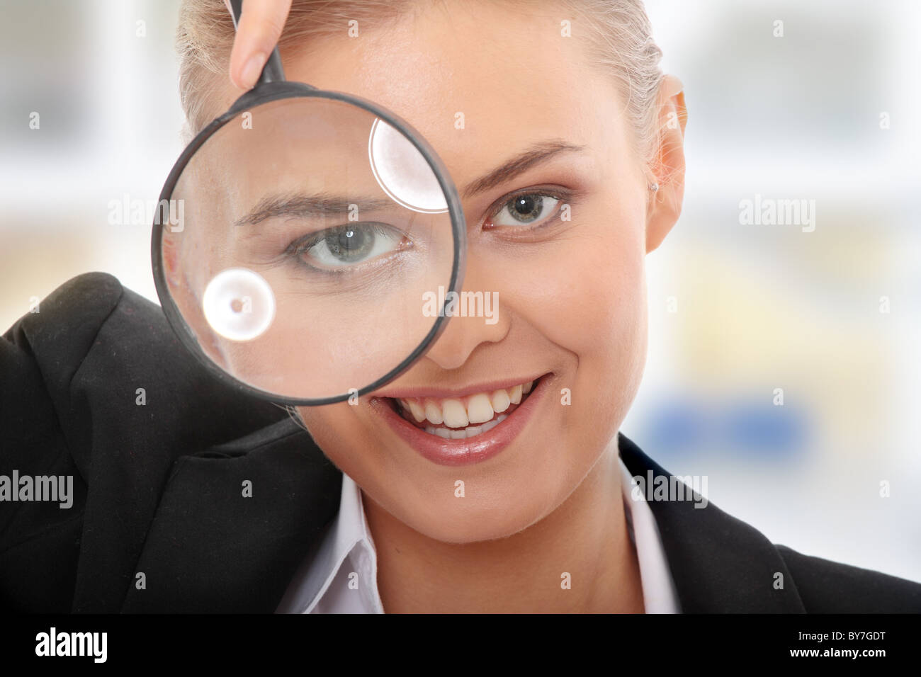 Young attractive smiling business woman looking into a magnifying glass ...