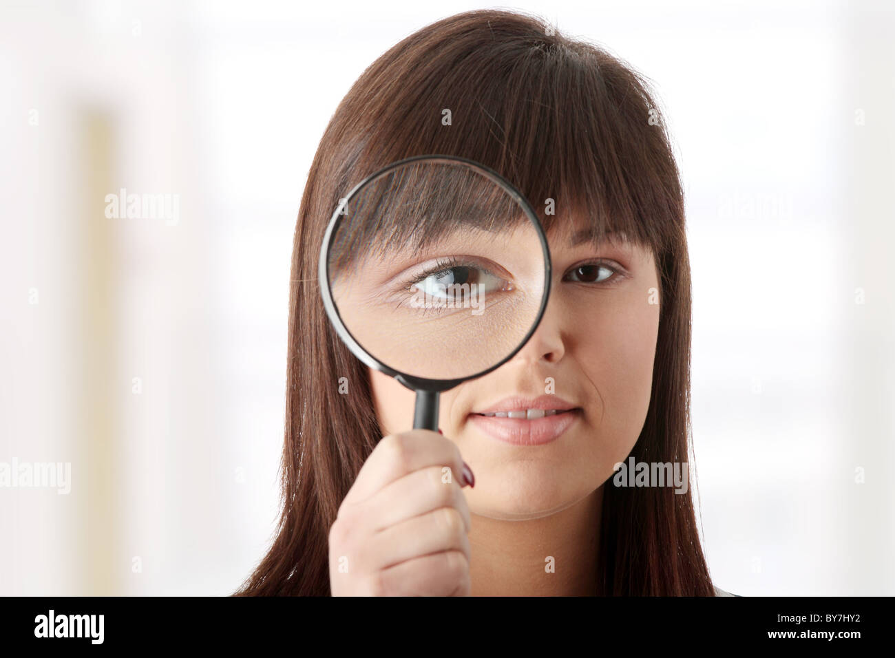 Young attractive smiling business woman looking into a magnifying glass ...