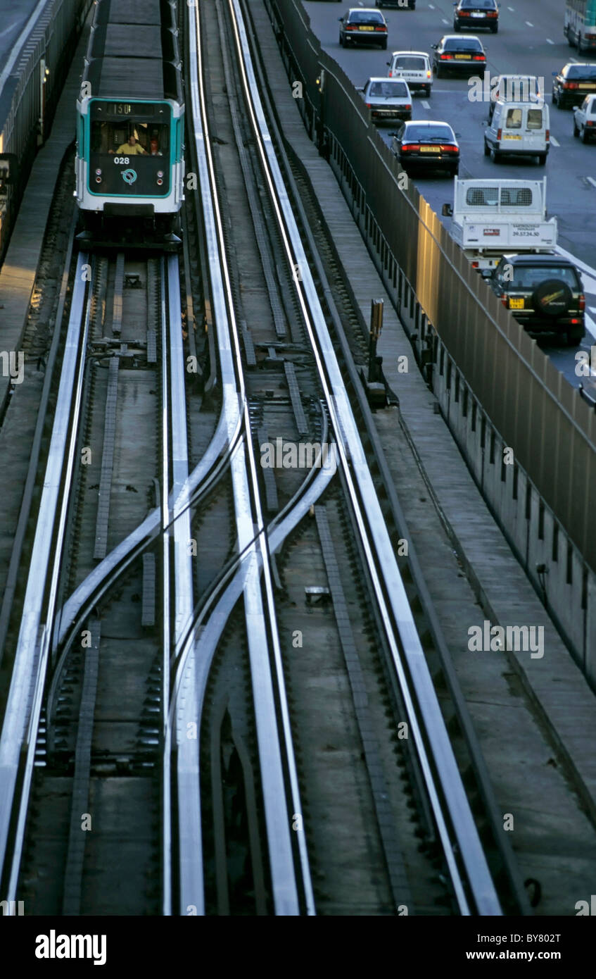 Man driving a subway train while looking across at traffic on the road ...