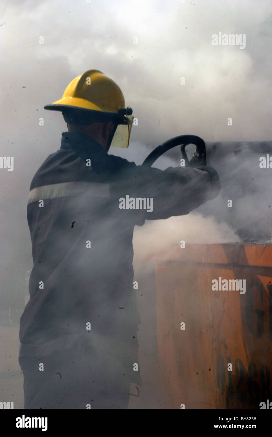 fireman using a hose on a small fire Stock Photo - Alamy