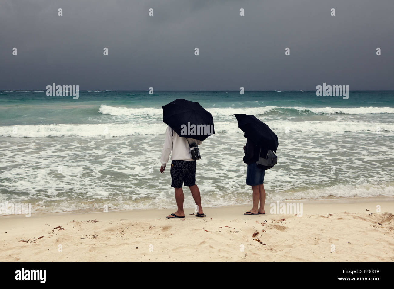 A couple walk along the beach on a stormy day at Tulum, Yucatan ...