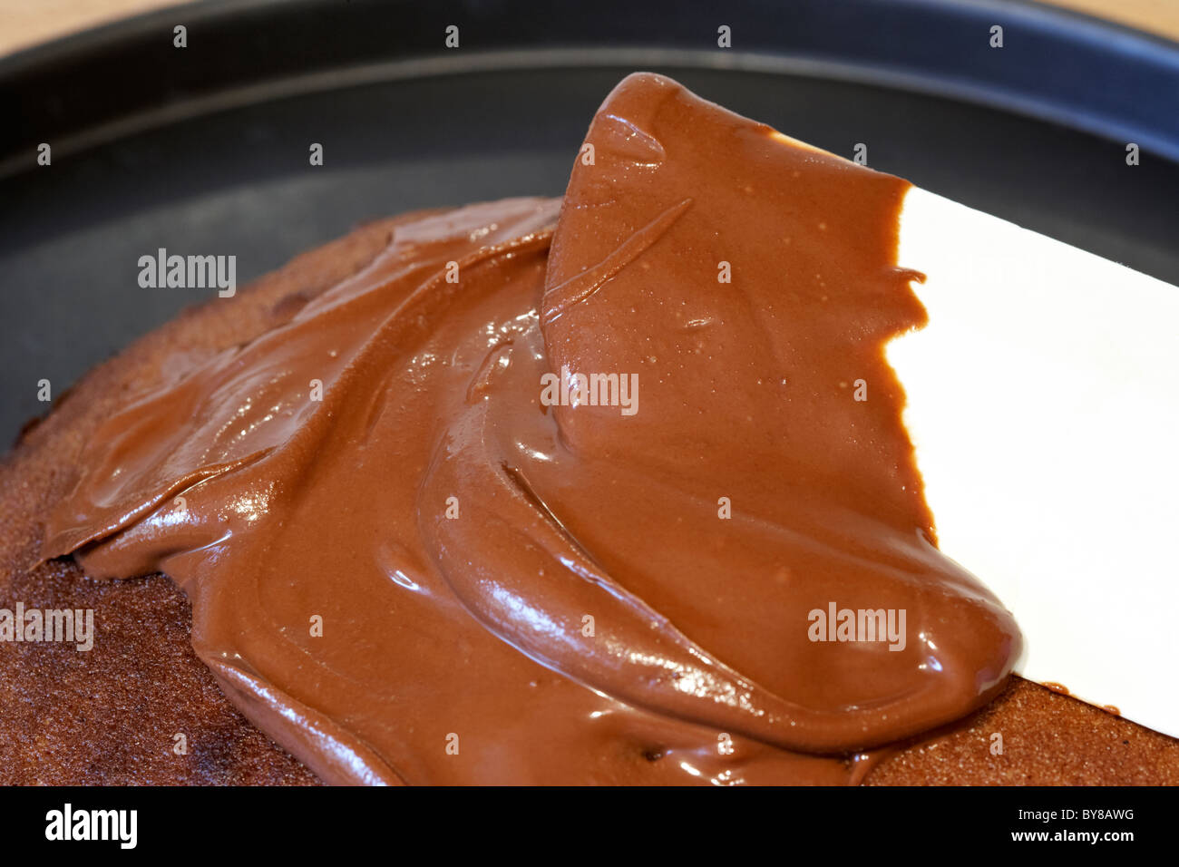 spreading chocolate coating on a homemade chocolate sponge cake with a ...