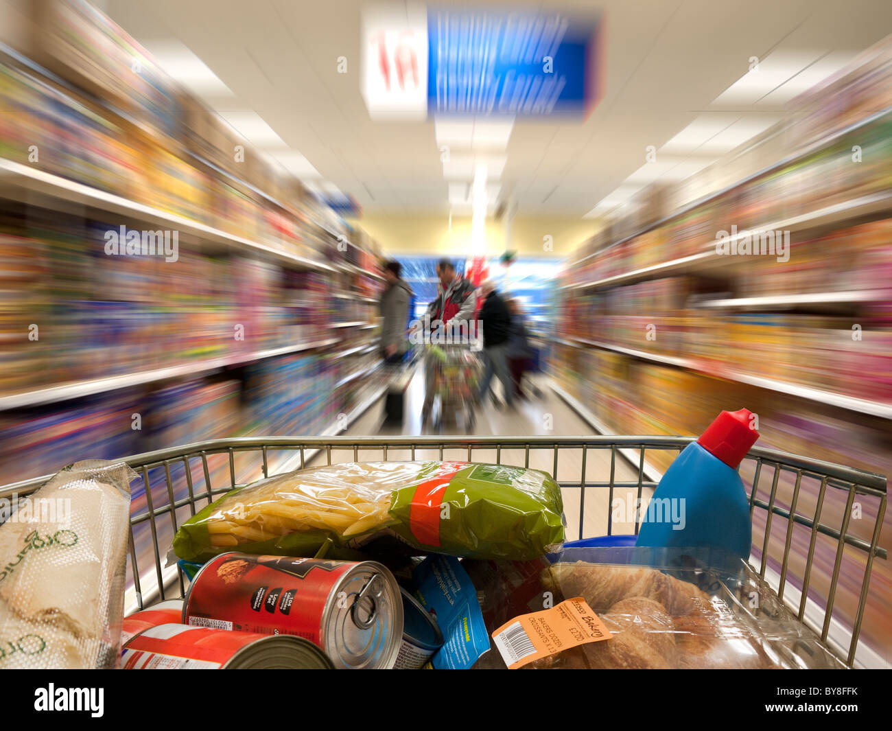view over a loaded supermarket trolley as it is pushed down an aisle ...