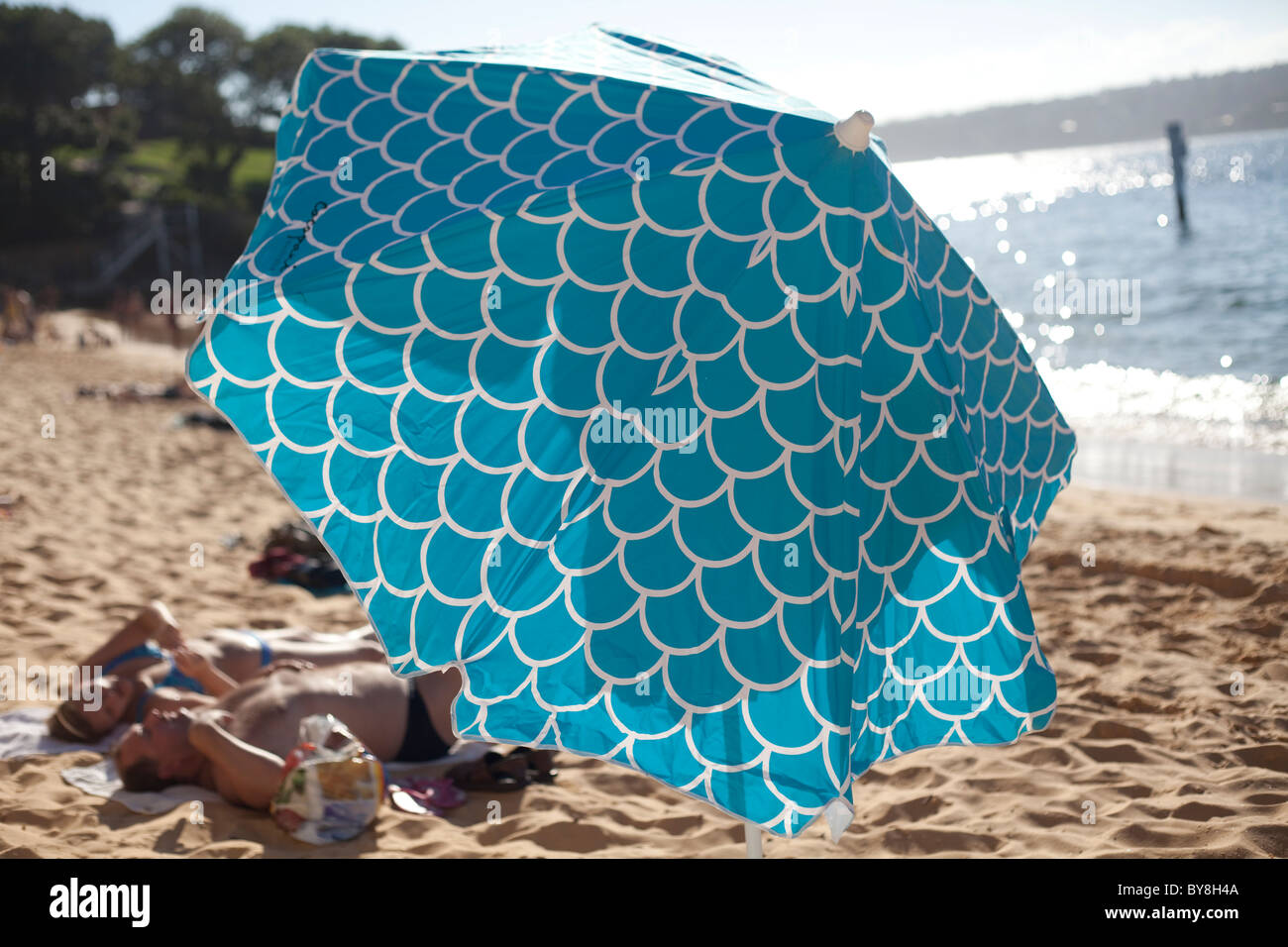 Sunbathers under a blue beach umbrella at Camp Cove beach in Watsons ...