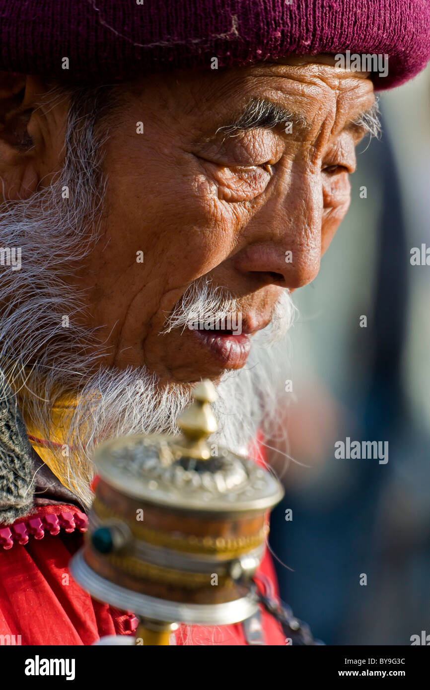 Old Tibetan man pilgrim with white beard and moustache spinning prayer ...