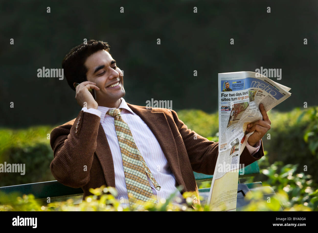 Businessman reading a newspaper while talking on a mobile phone Stock ...