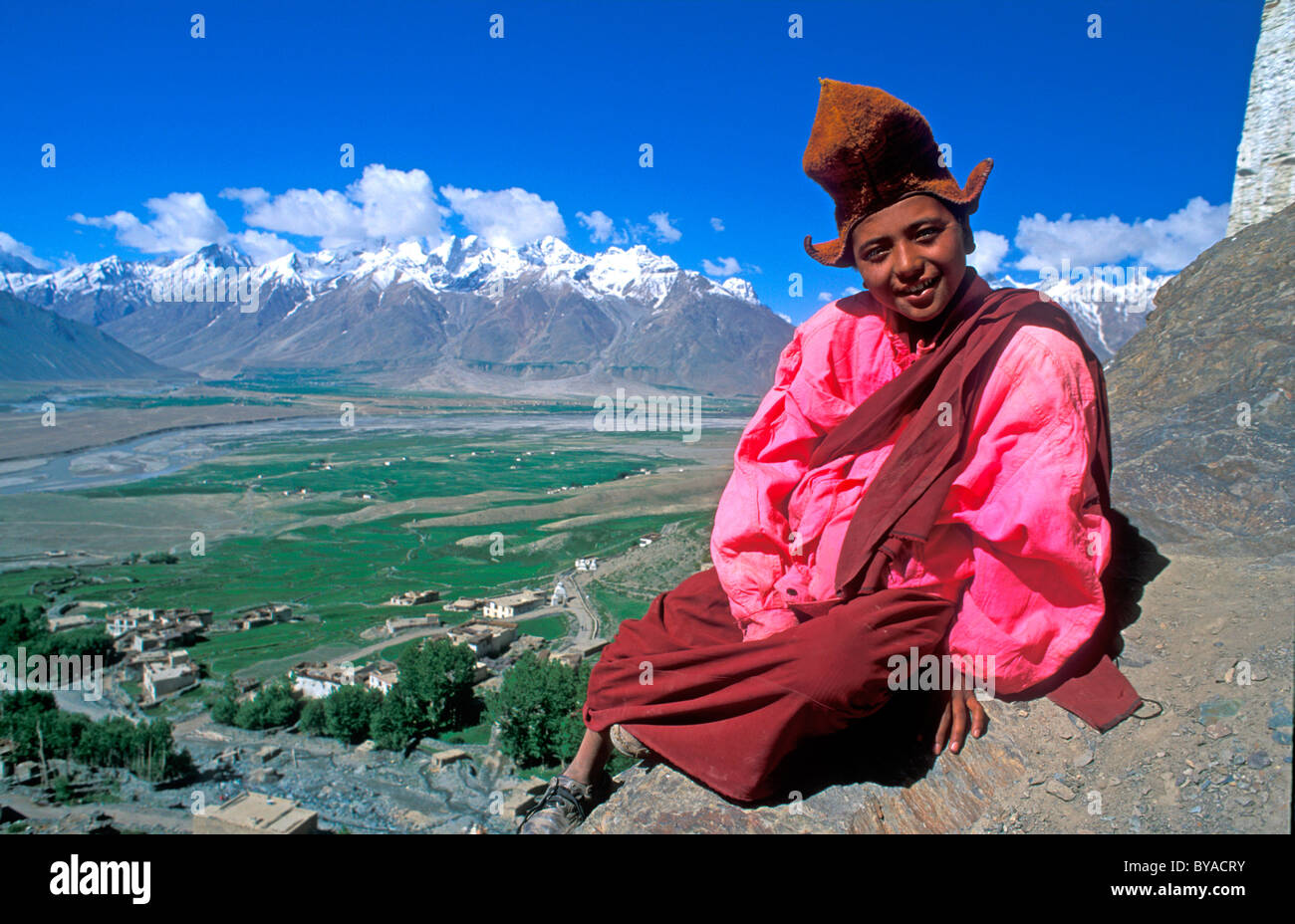 Young Buddhist monk wearing monk's robes sitting on a rock, in front of ...