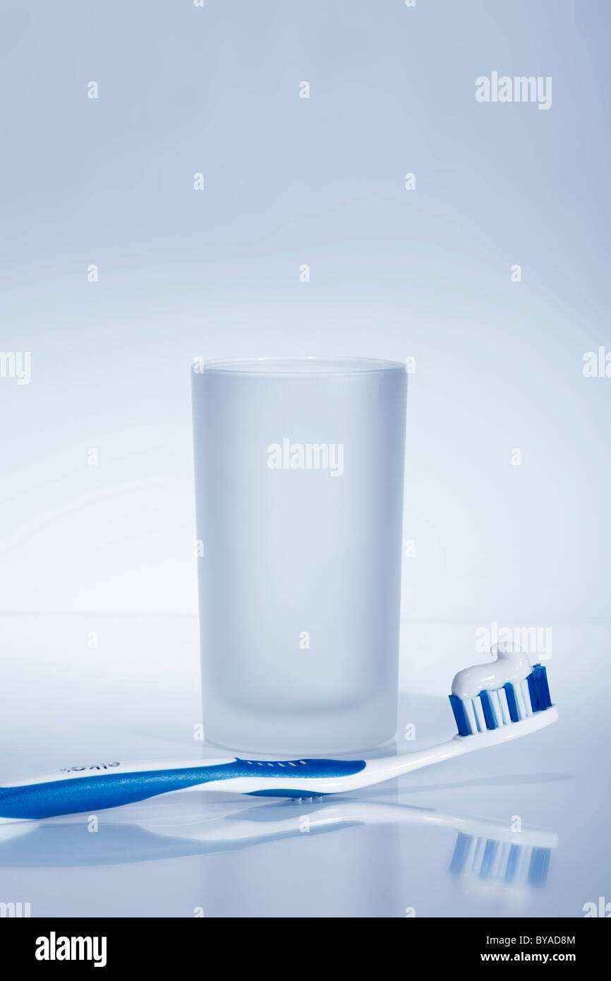 Blue and white toothbrush with toothpaste in front of a water glass ...