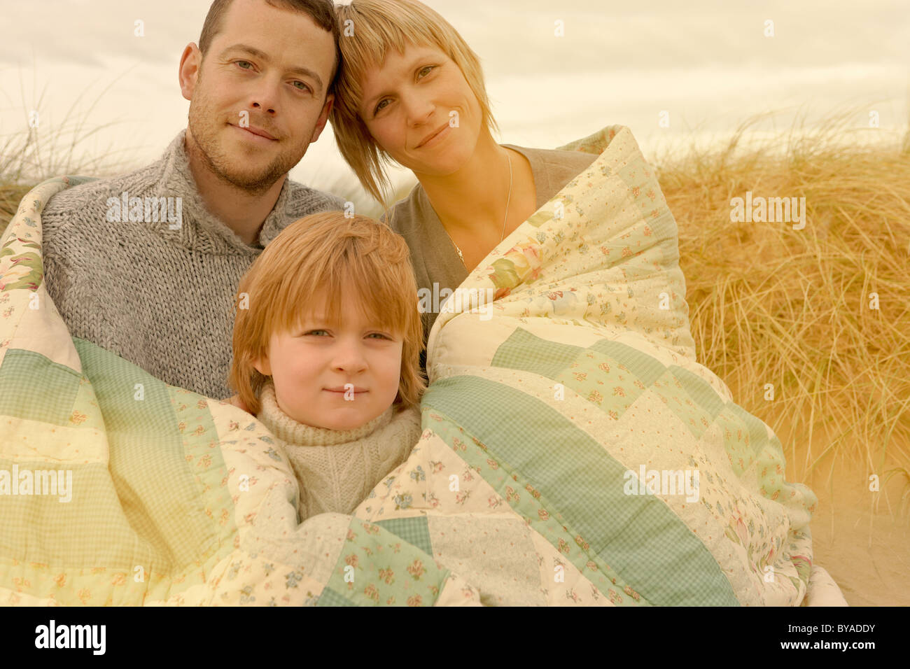 Family cuddling under quilt on beach Stock Photo - Alamy