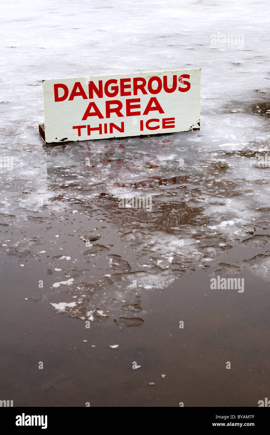 A pond covered in a thin layer of ice with some open water, and a sign ...