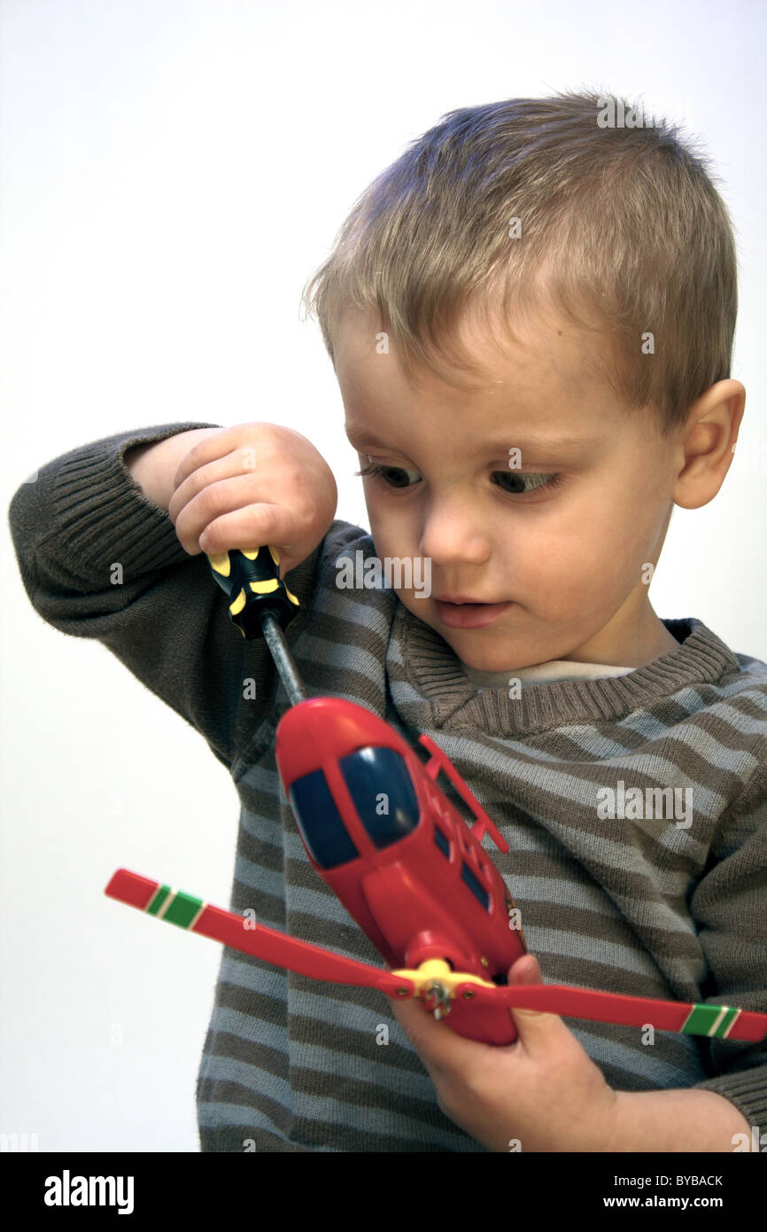 A young Caucasian male toddler mending his broken toy helicopter with a ...