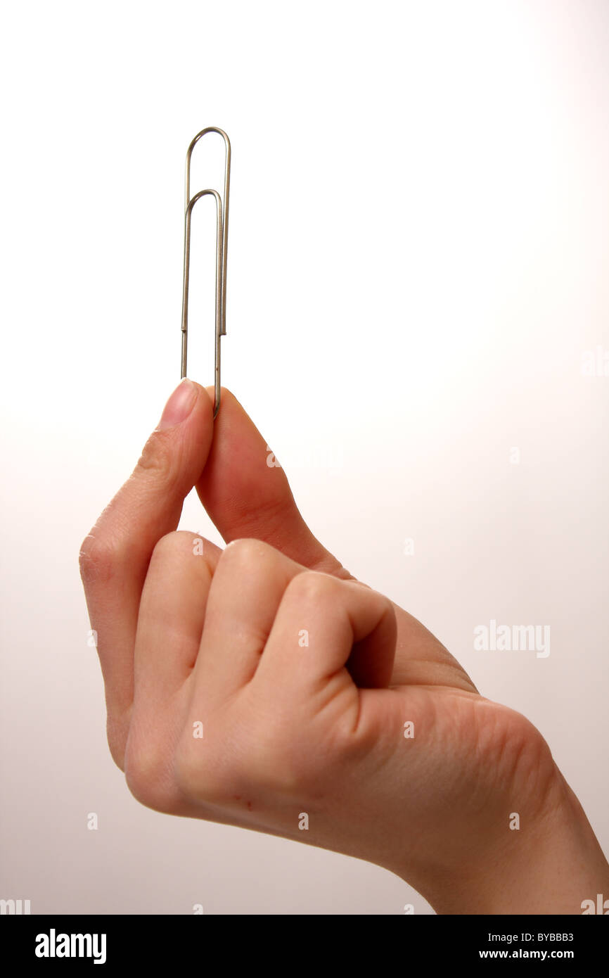 A large paper clip held upright on a white background by a Caucasian ...