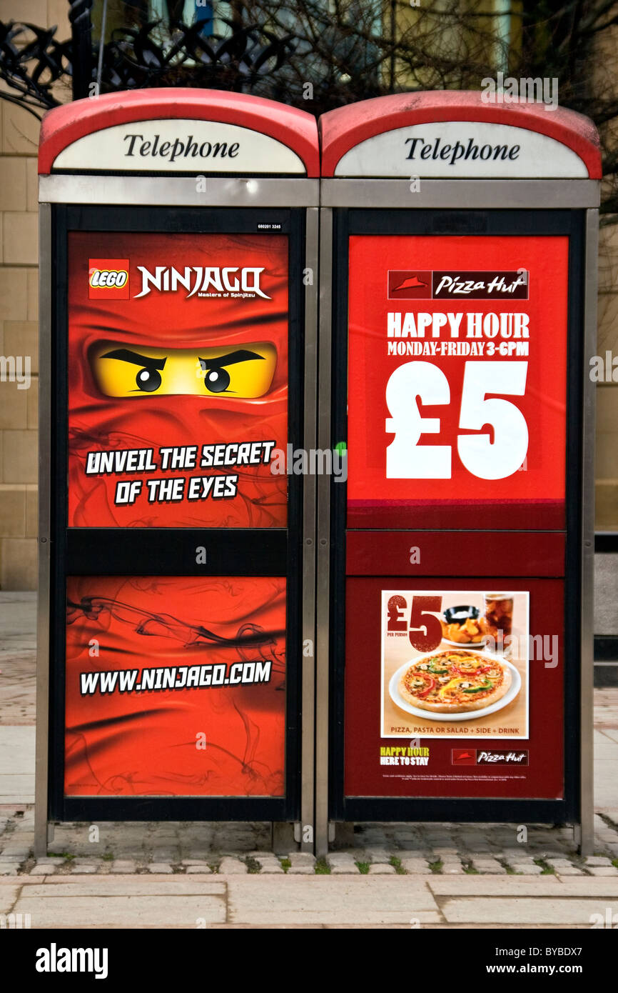 Two public BT Telephone boxes with advertisement posters covering the ...