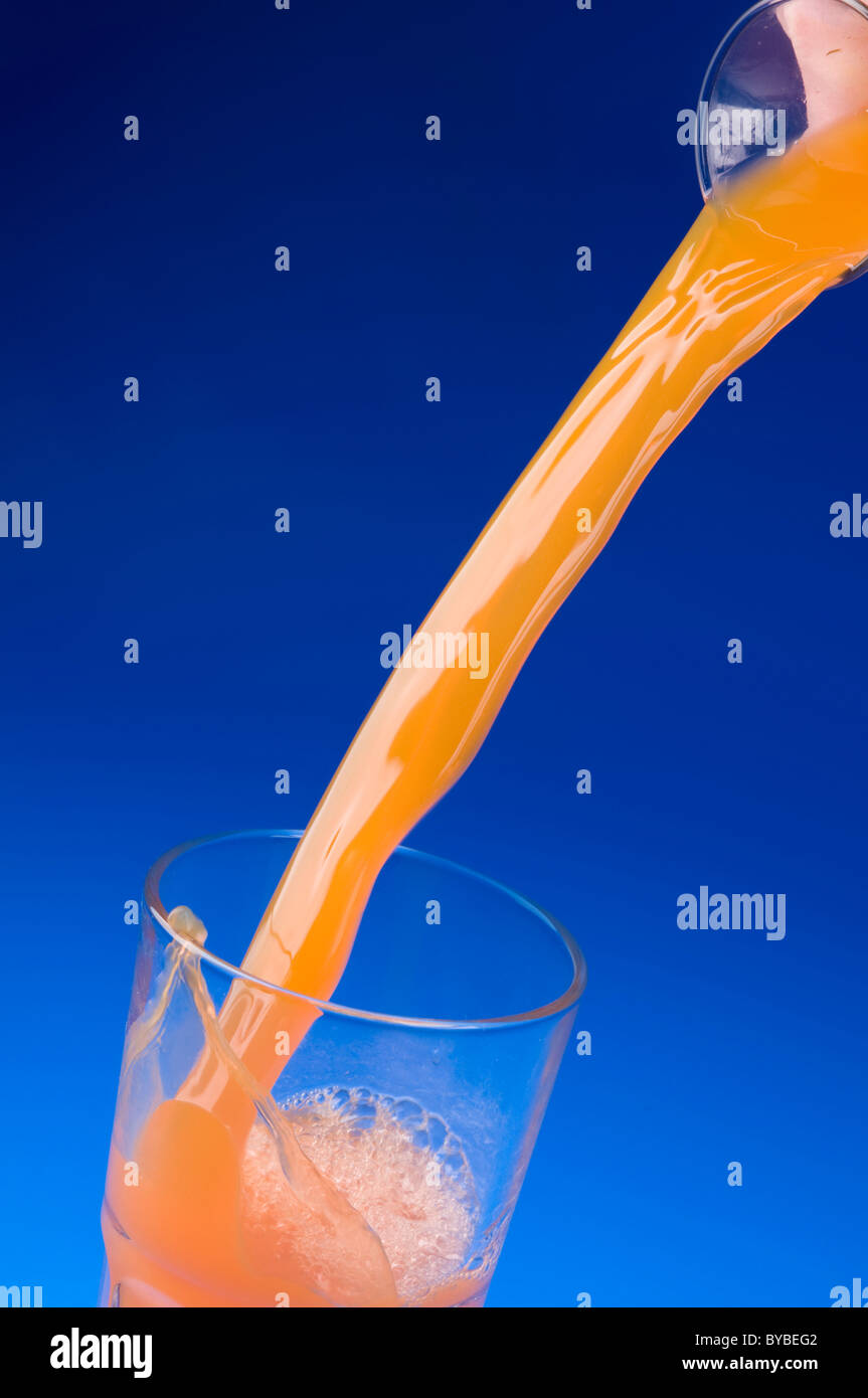 Stream of fresh orange juice over blue background Stock Photo - Alamy