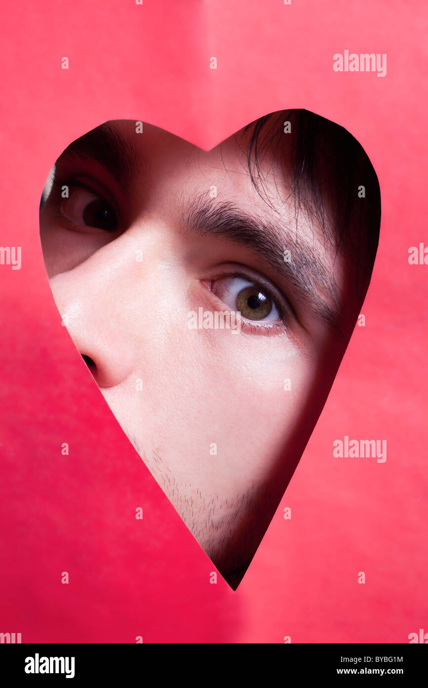 Face of young man peering from hole in heart-shaped Stock Photo - Alamy
