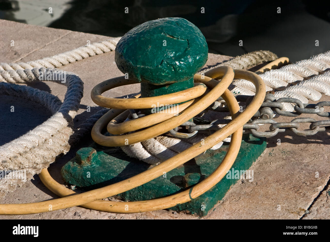 Green mooring bollard with rope and hose pipe Stock Photo - Alamy