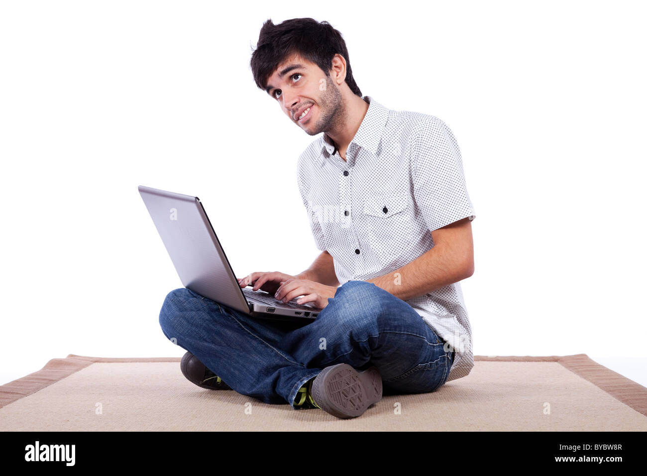 young man surfing the internet in his laptop sited on the carpet ...