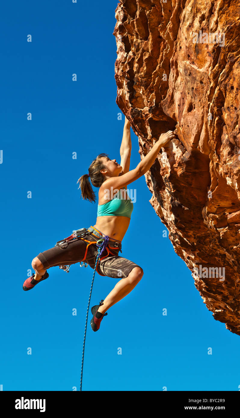 Female rock climber struggles for her next grip dangling on the edge of ...