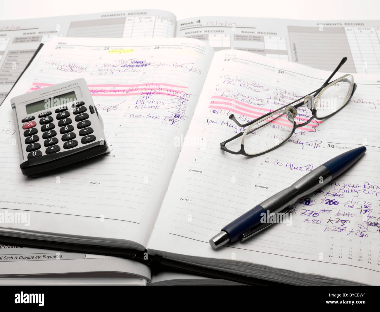 Calculator, reading glasses and a pen on top of a diary and accounts ...