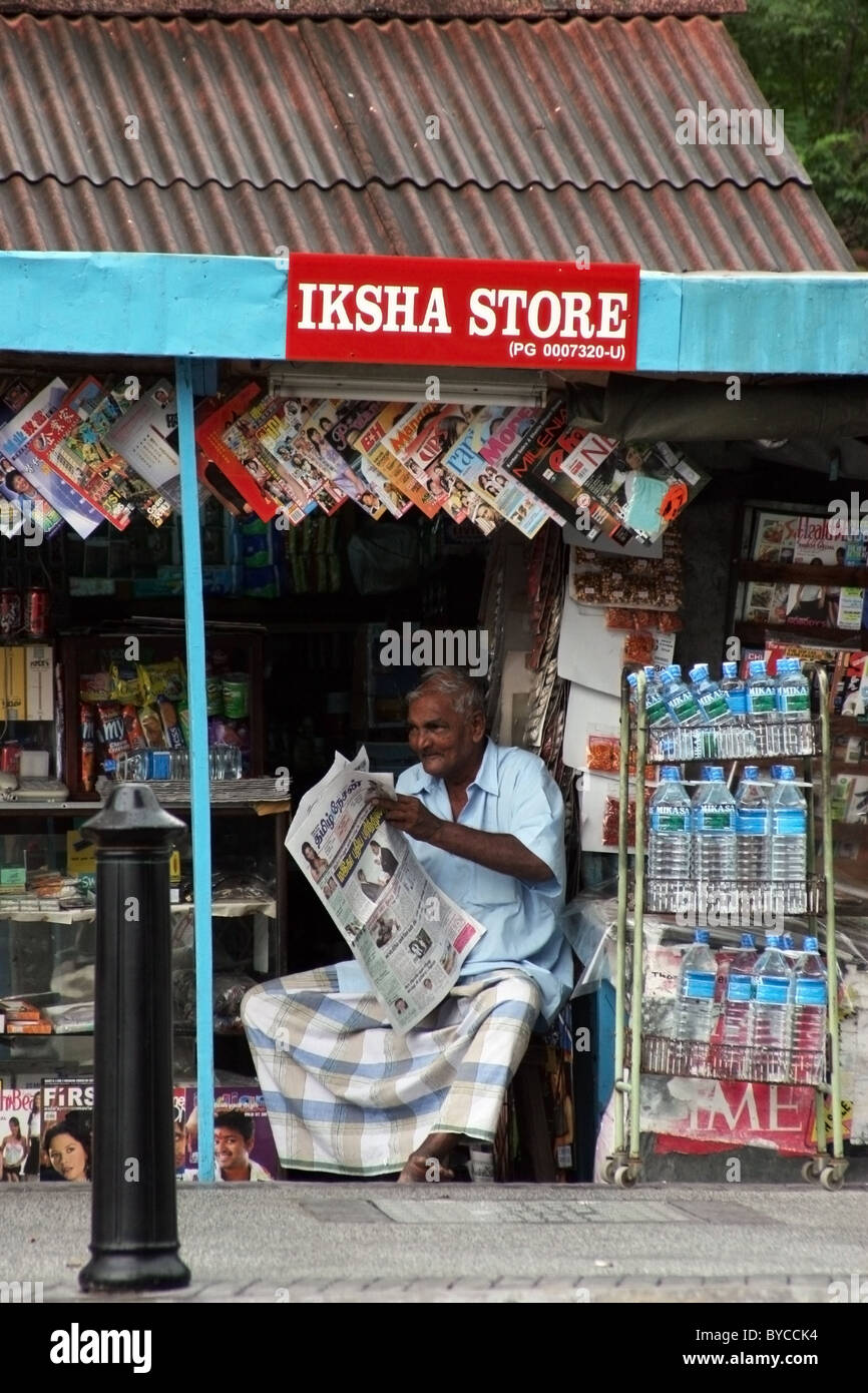 A literate Asian man is reading a Malaysian newspaper in a small ...