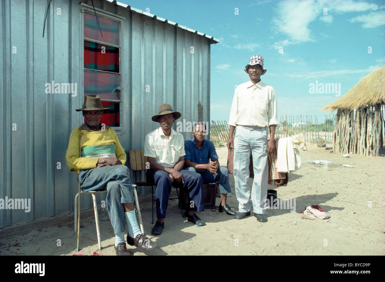San men sitting outside government built housing in Tchumkwe, Bushman ...