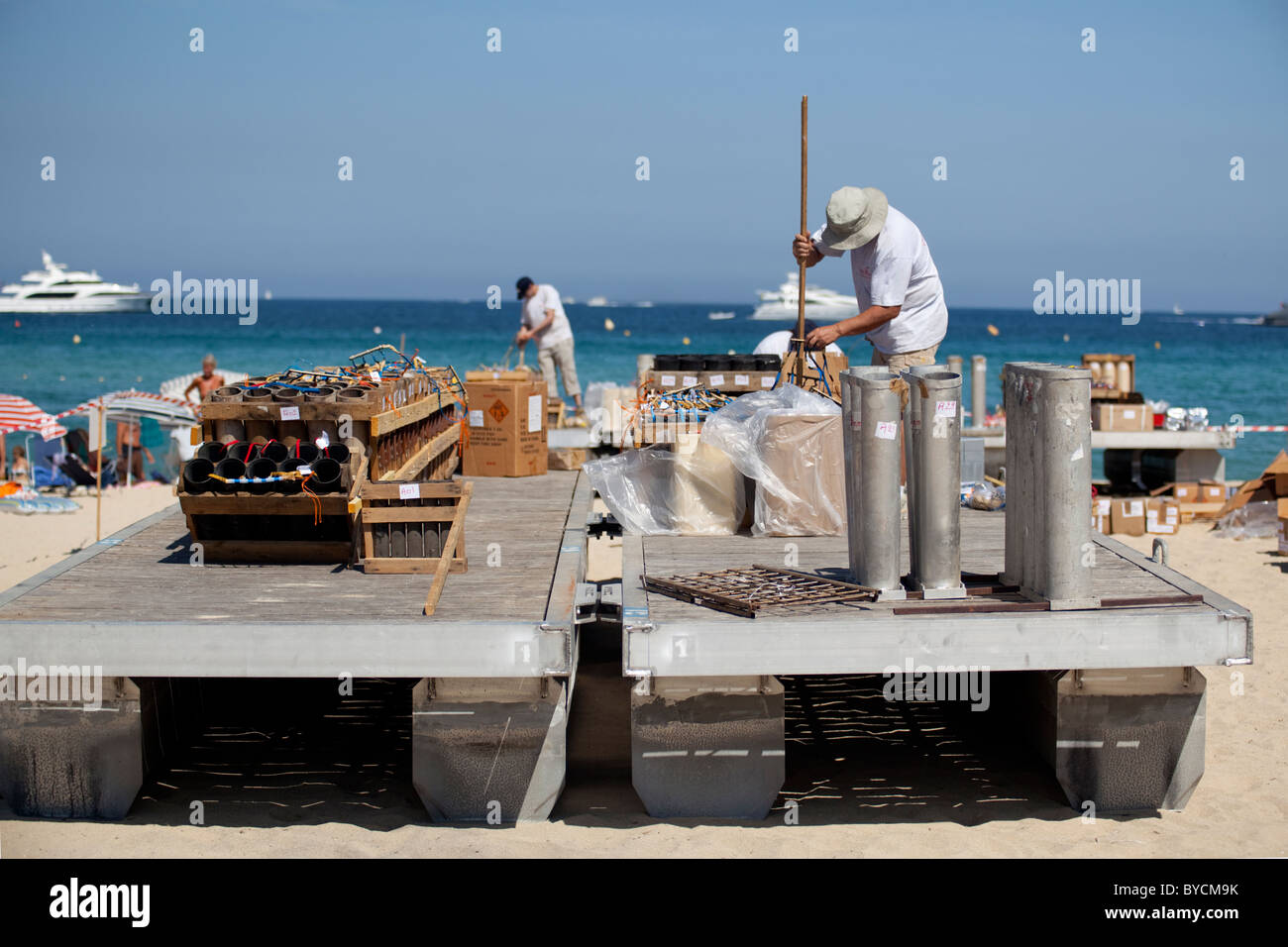 Men installing firework bombs on a floating raft laying on the sand for ...