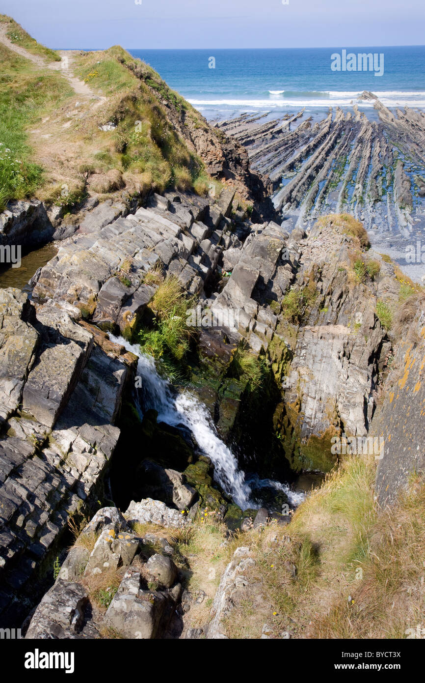 A little stream forces its way over vertical rock strata in a waterfall ...