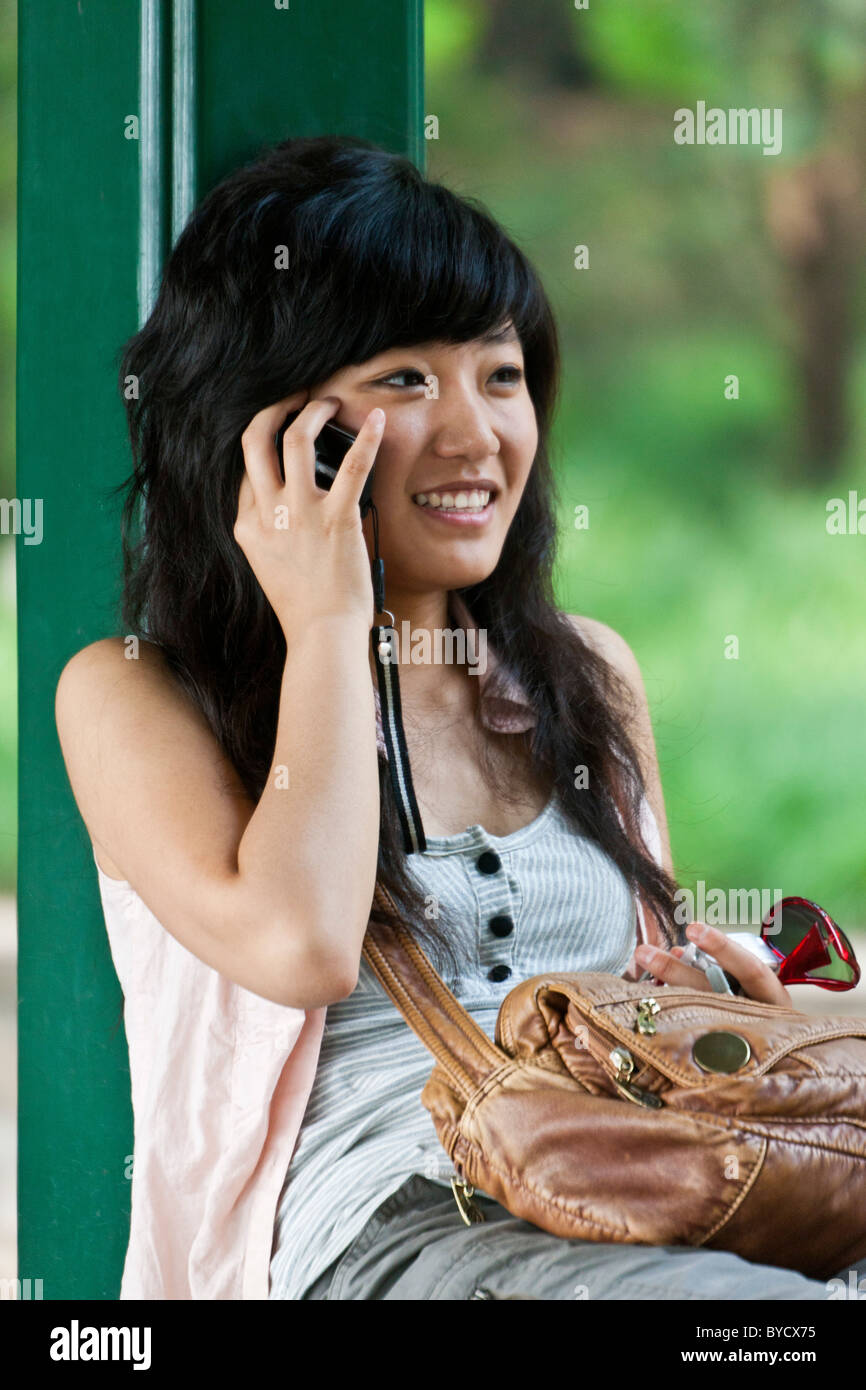 Attractive young Chinese woman speaking on cellphone in the grounds of ...