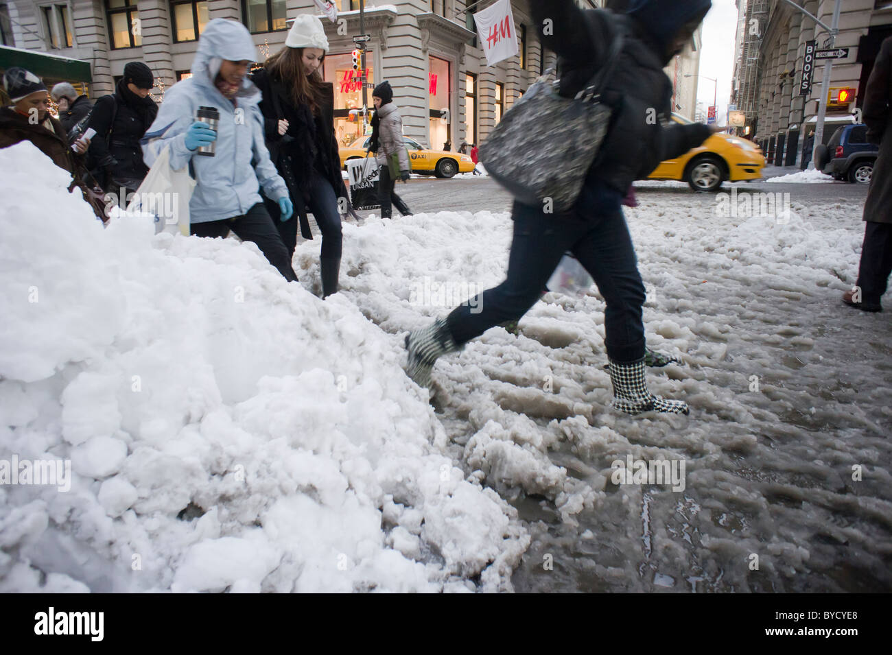 Pedestrians maneuver through puddles of slush and piles of snow at a ...