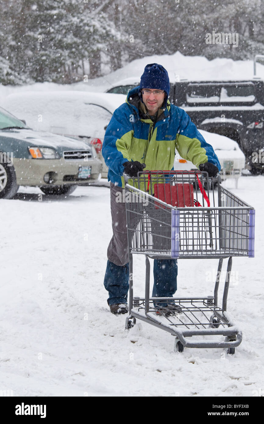 Man pushes shopping cart in winter snowstorm parking lot of grocery ...