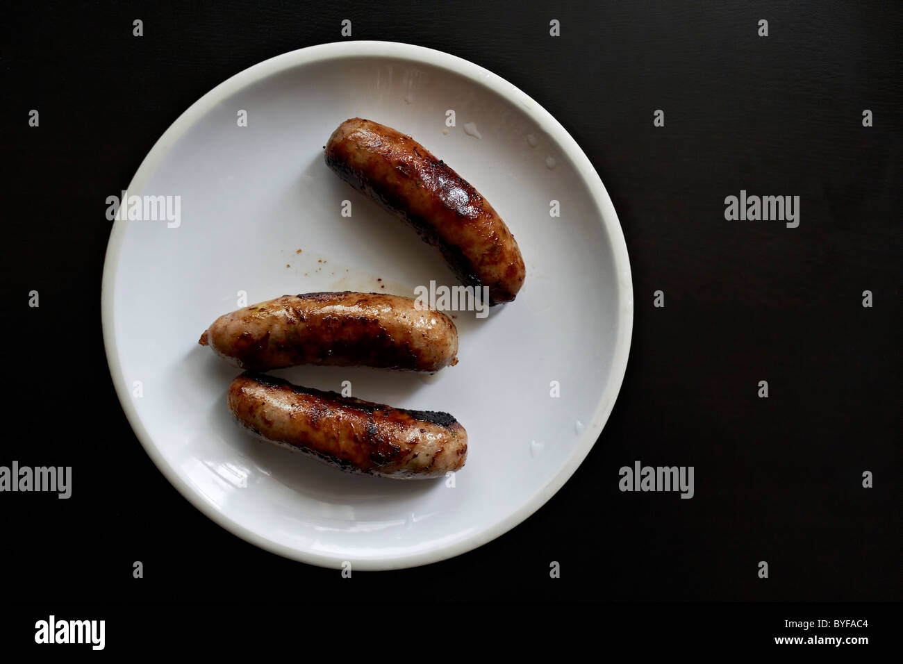 Three perfectly cooked pork sausages on a white dinner plate, ready to ...