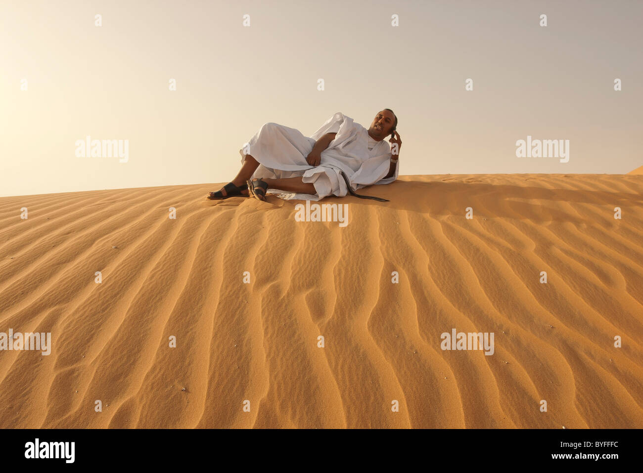 Mauritanian Arab man in traditional dress sits on a Saharan sand dune ...