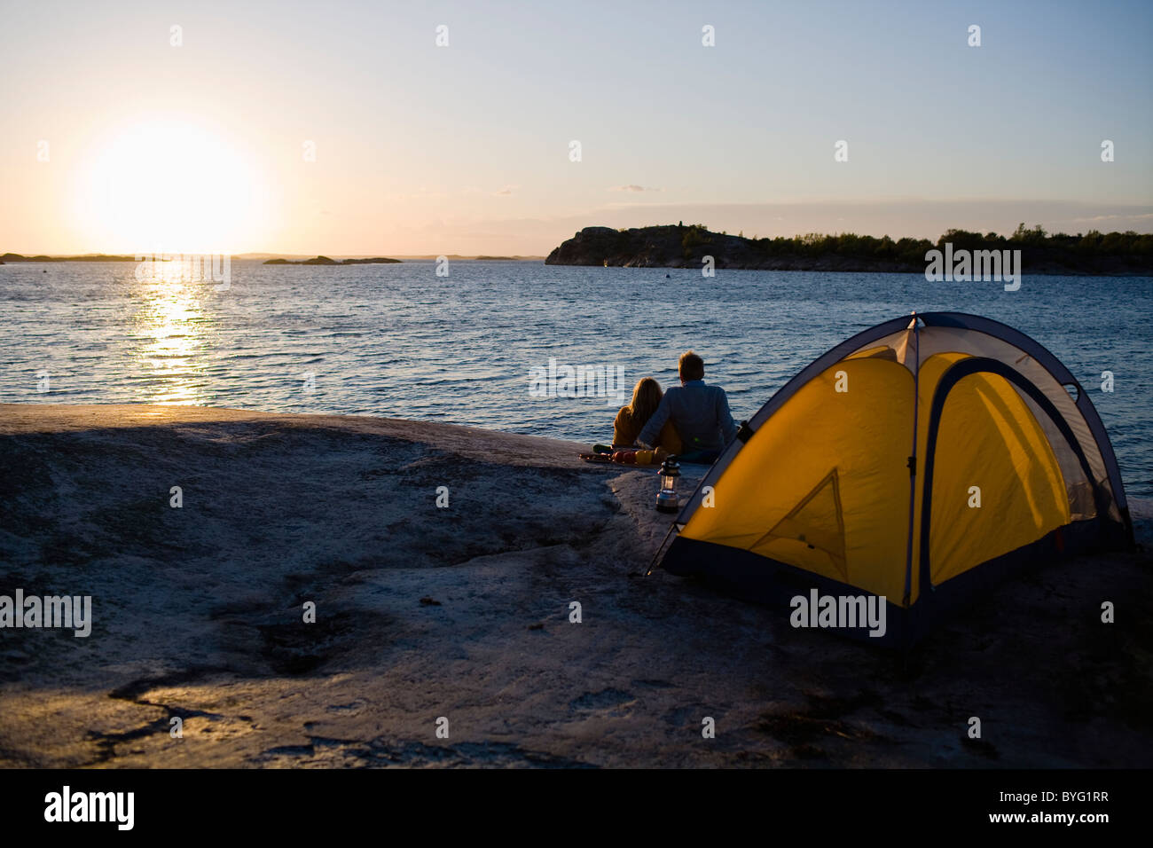 Couple camping by sea at sunset Stock Photo - Alamy