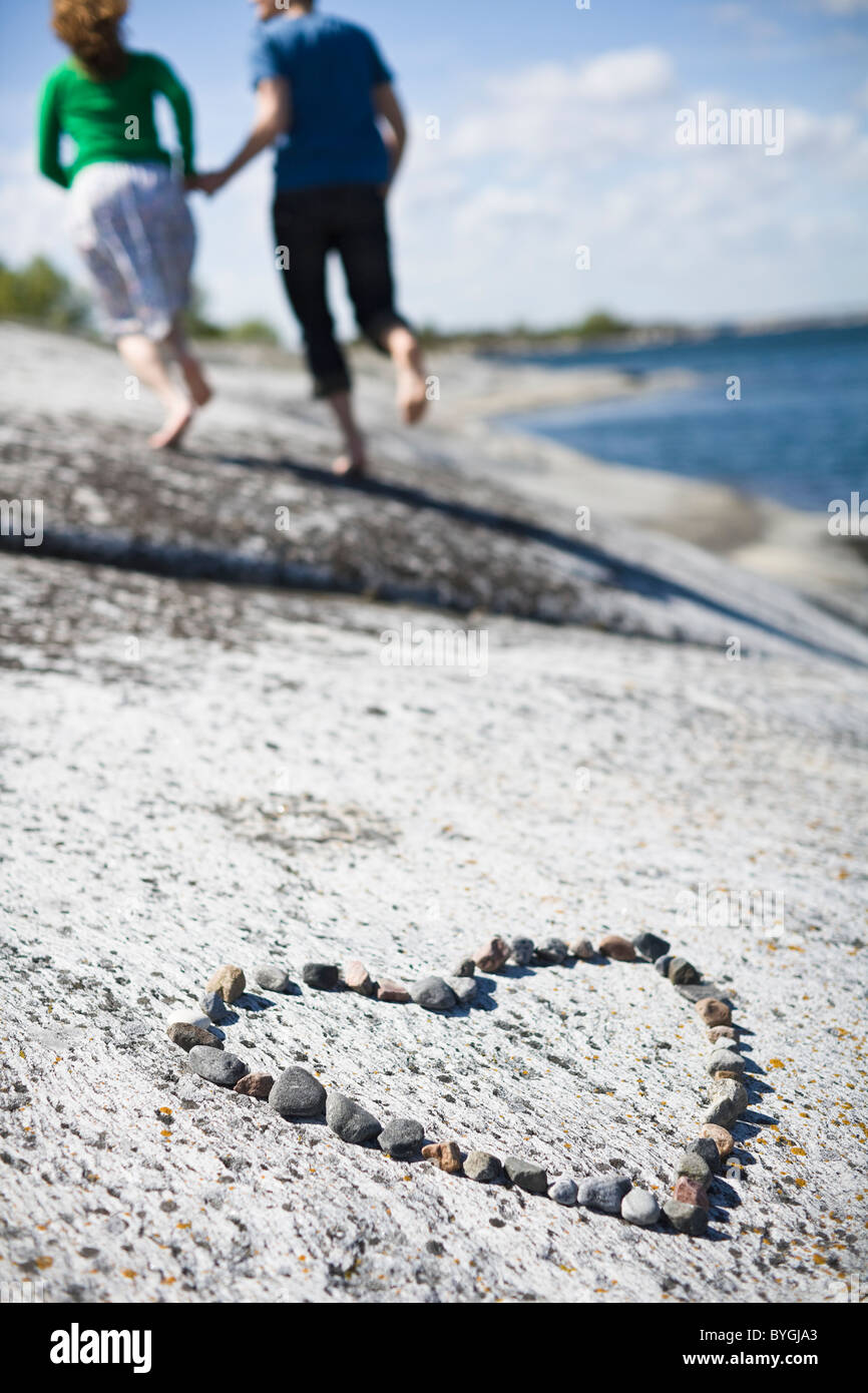 Pebbles in shape of heart on beach, running couple in the background ...