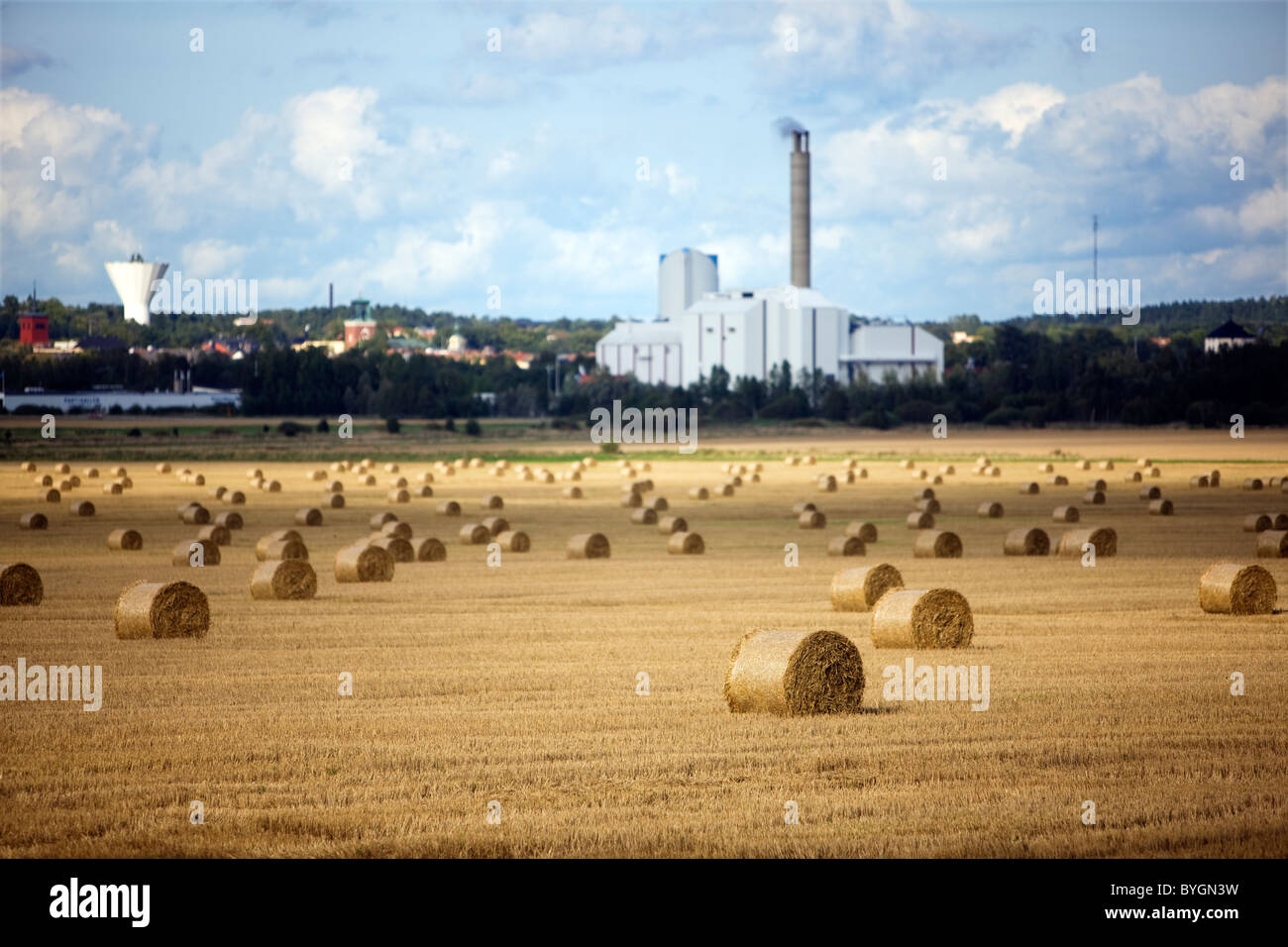 Hay bales in field with factory in distance Stock Photo - Alamy