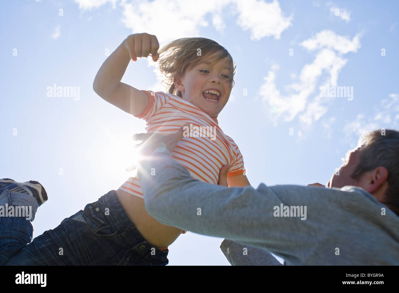 Low-angle view father lifting son in bright sunlight, backlit Stock ...