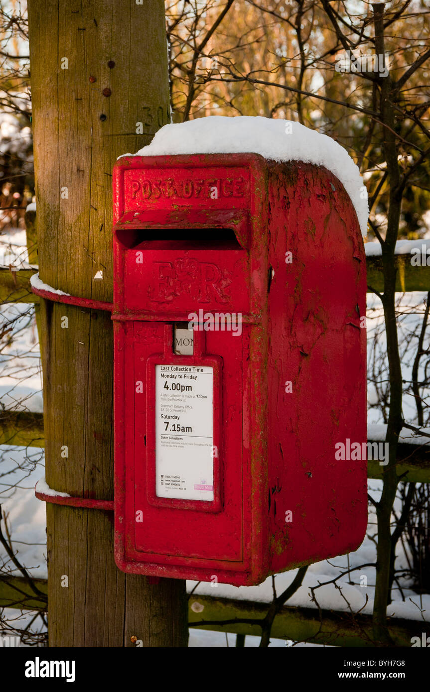A snow covered red letter box fixed to a post in an English country ...