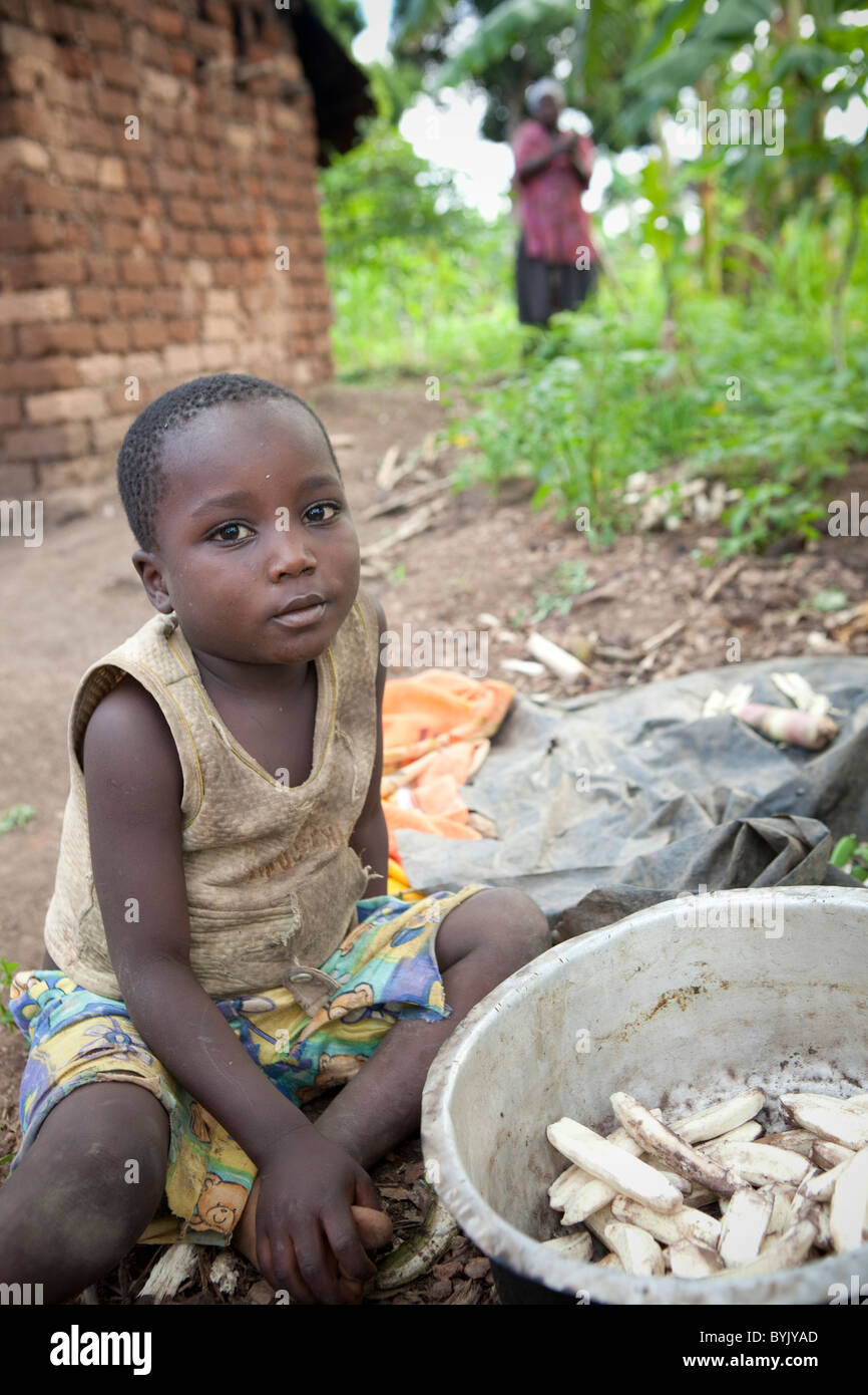 A young boy sits by a cooking pot full of bananas in rural Masaka ...