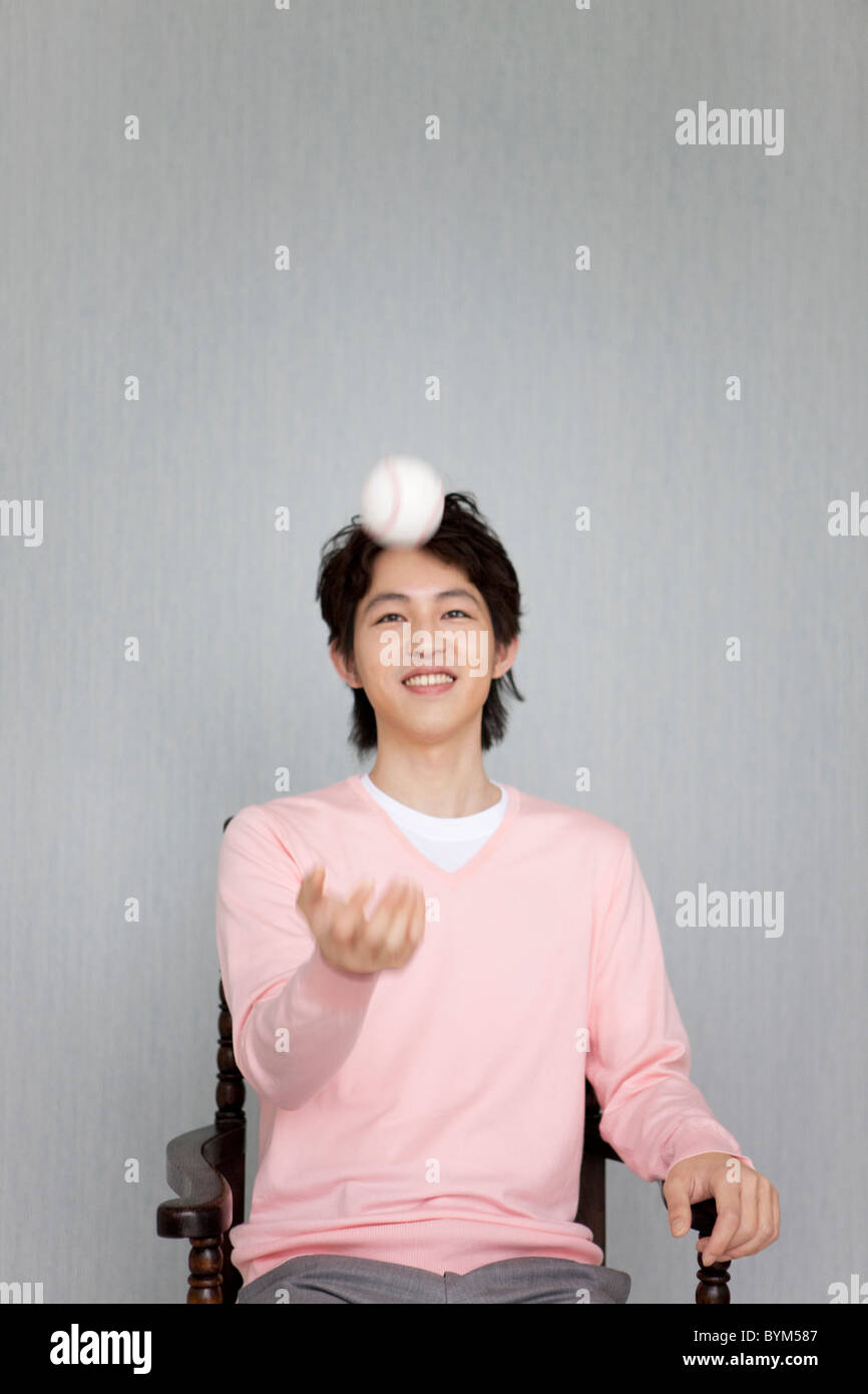 Young man sitting on chair throwing baseball Stock Photo - Alamy