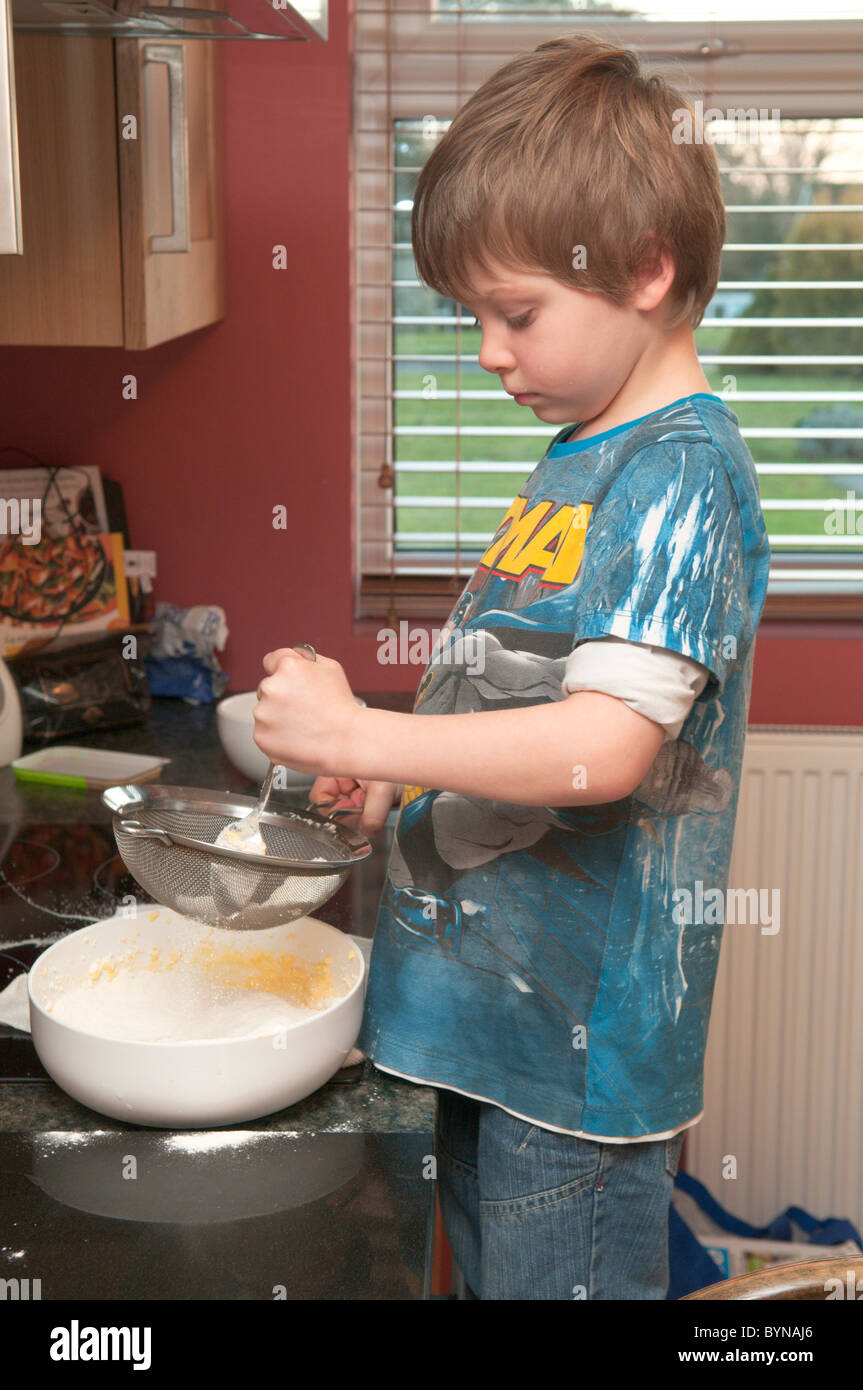 boy, child in kitchen sieving ingredients into mixing bowl making a ...
